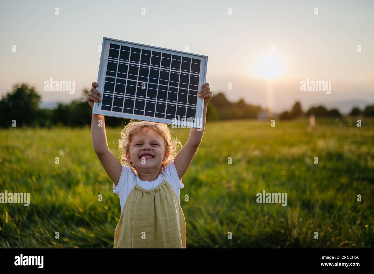 Little girl with model of solar panel, standing in the middle of meadow ...