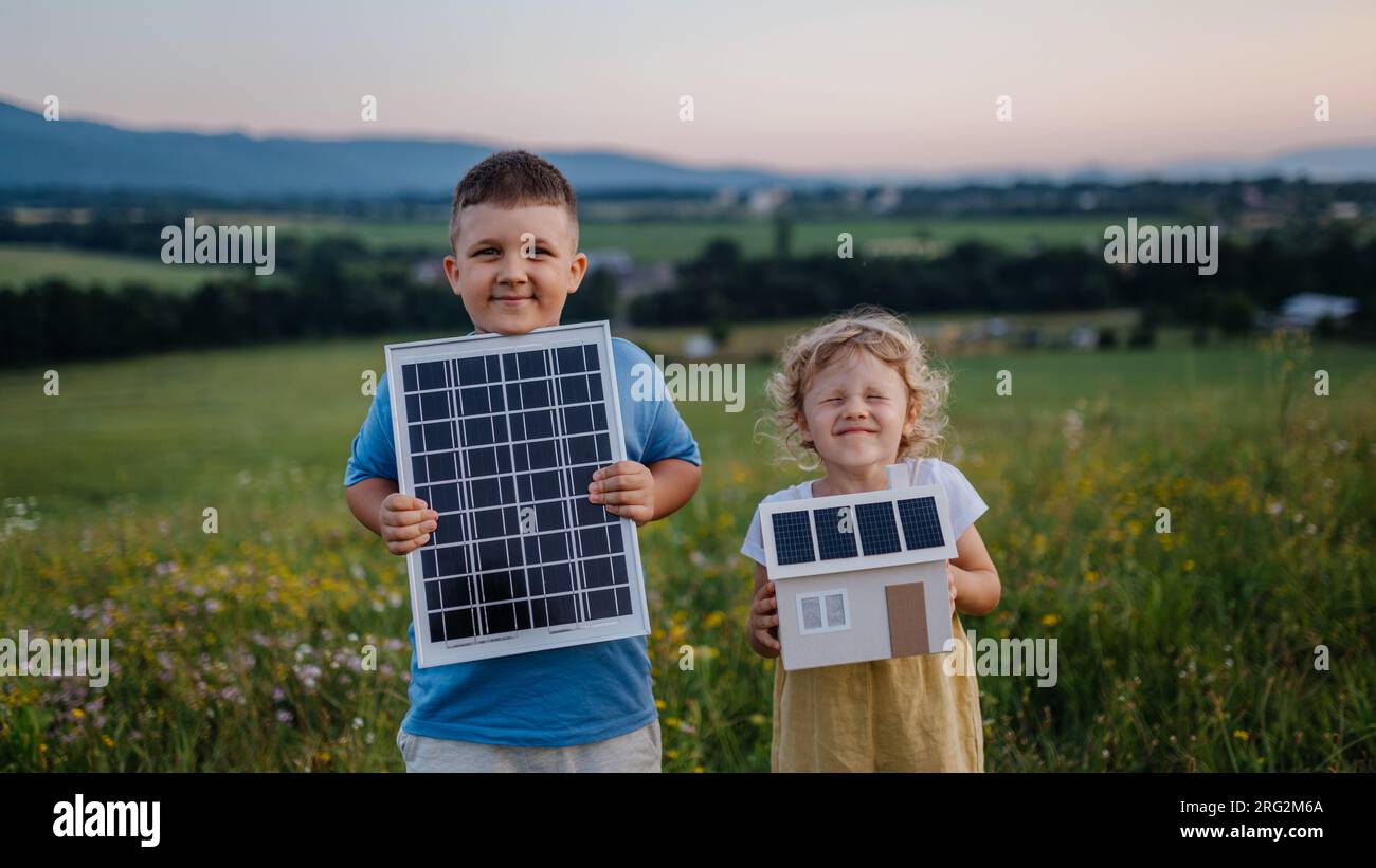 Young boy holding solar panel and his sister holding model of house ...