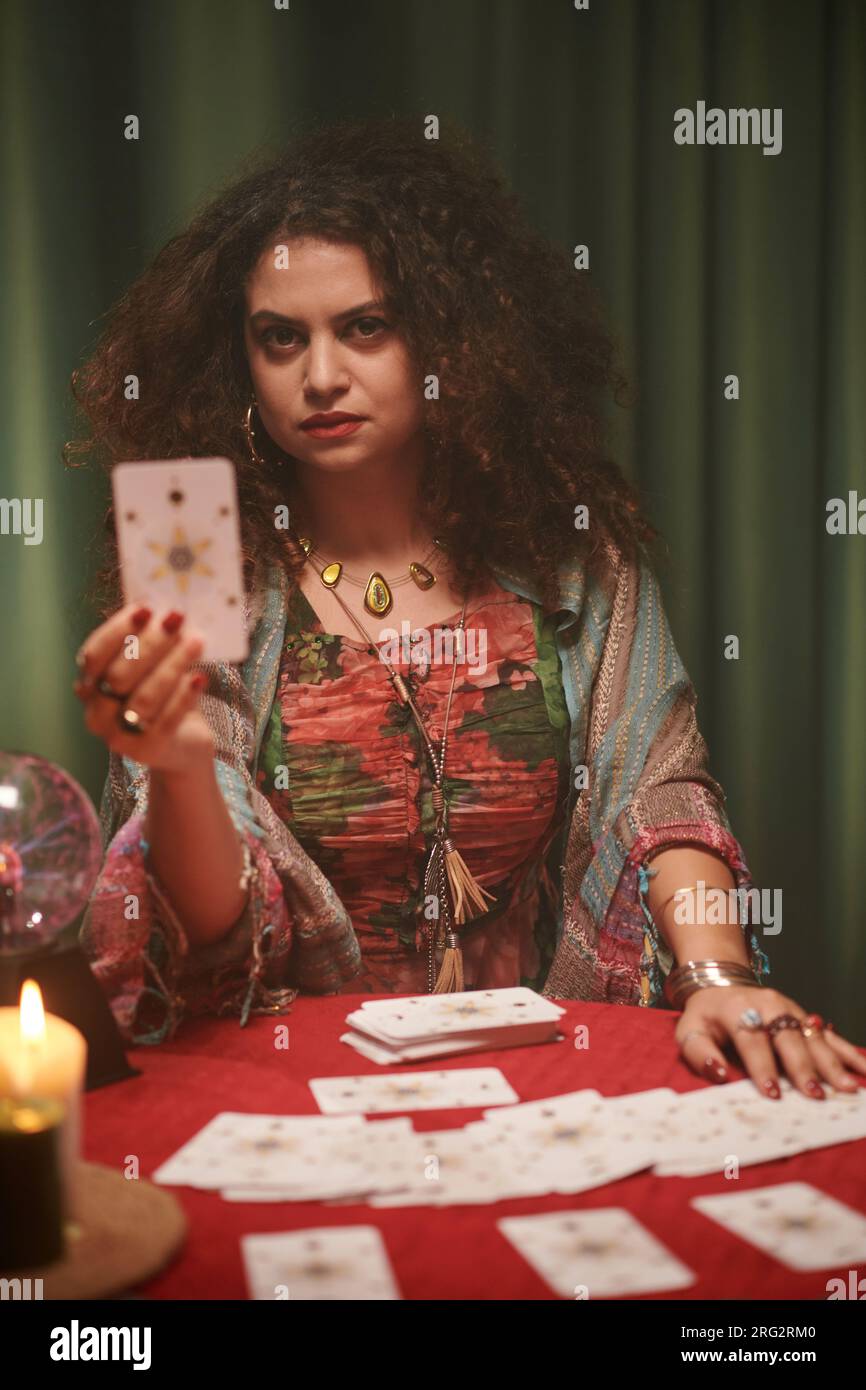 Portrait of serious fortune teller showing tarot card, warning client ...