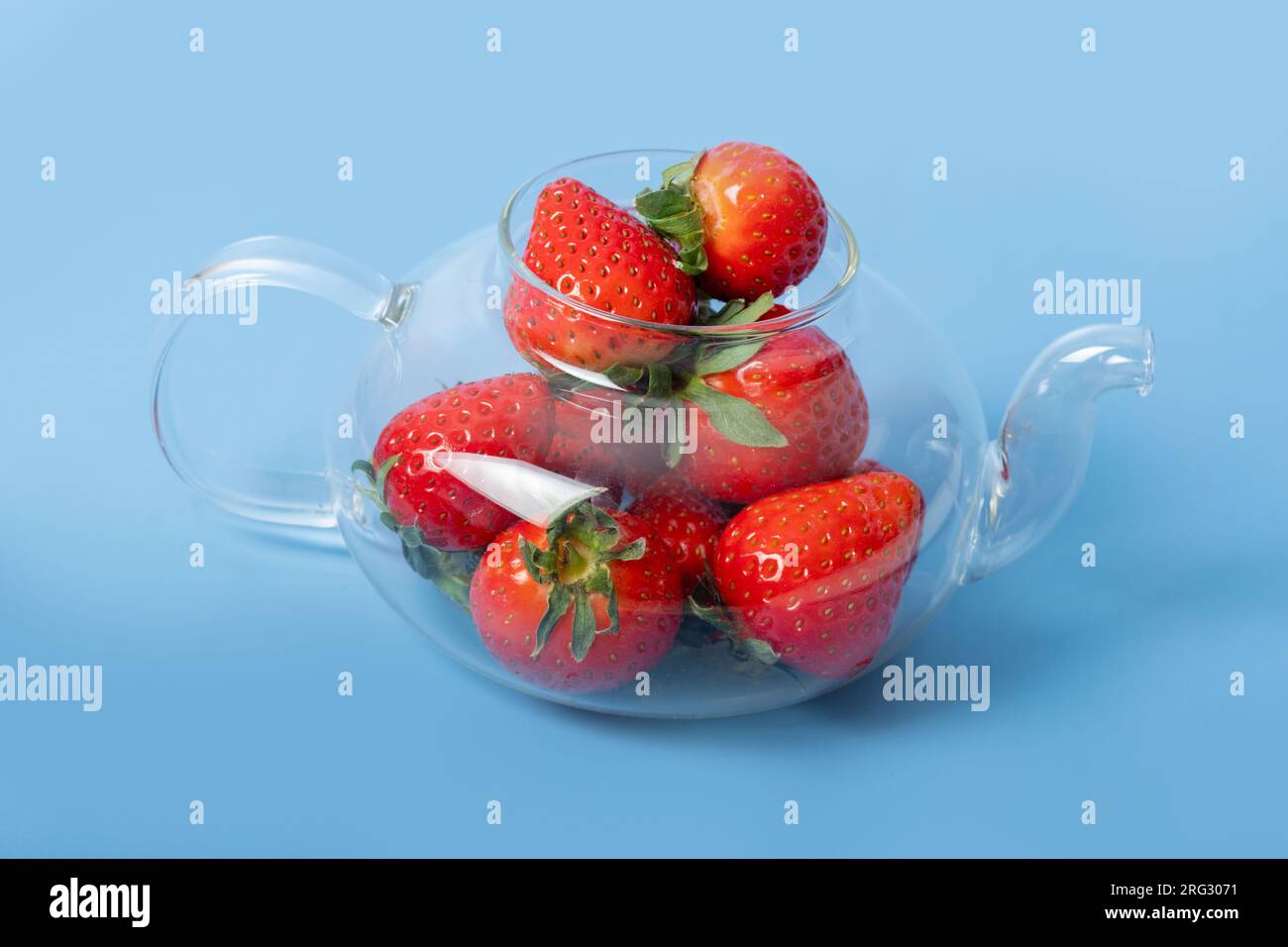Glass transparent teapot full of red ripe strawberries on a blue ...