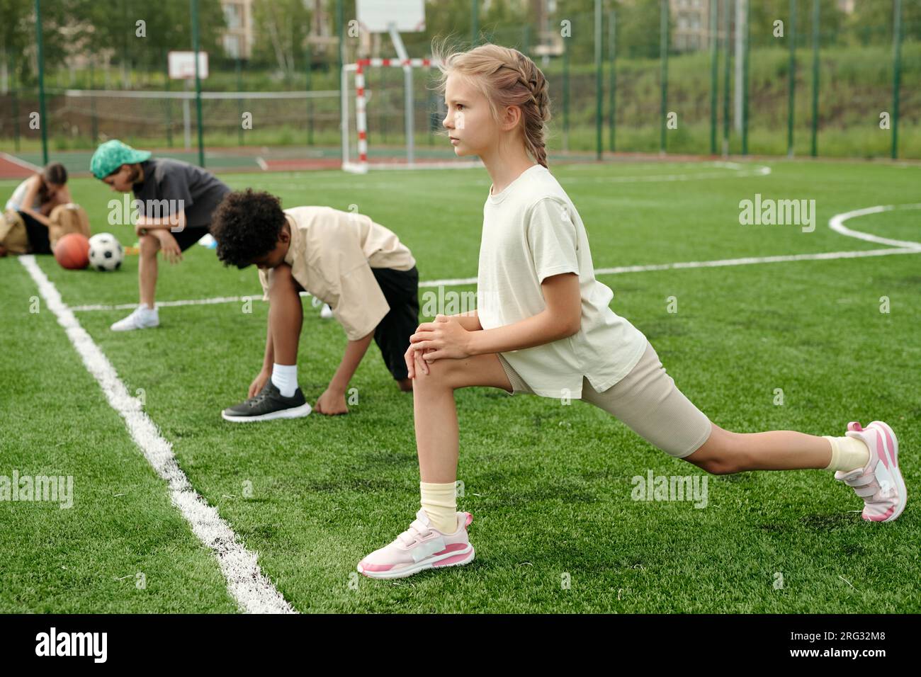 Side view of cute blond schoolgirl in activewear doing stretching ...