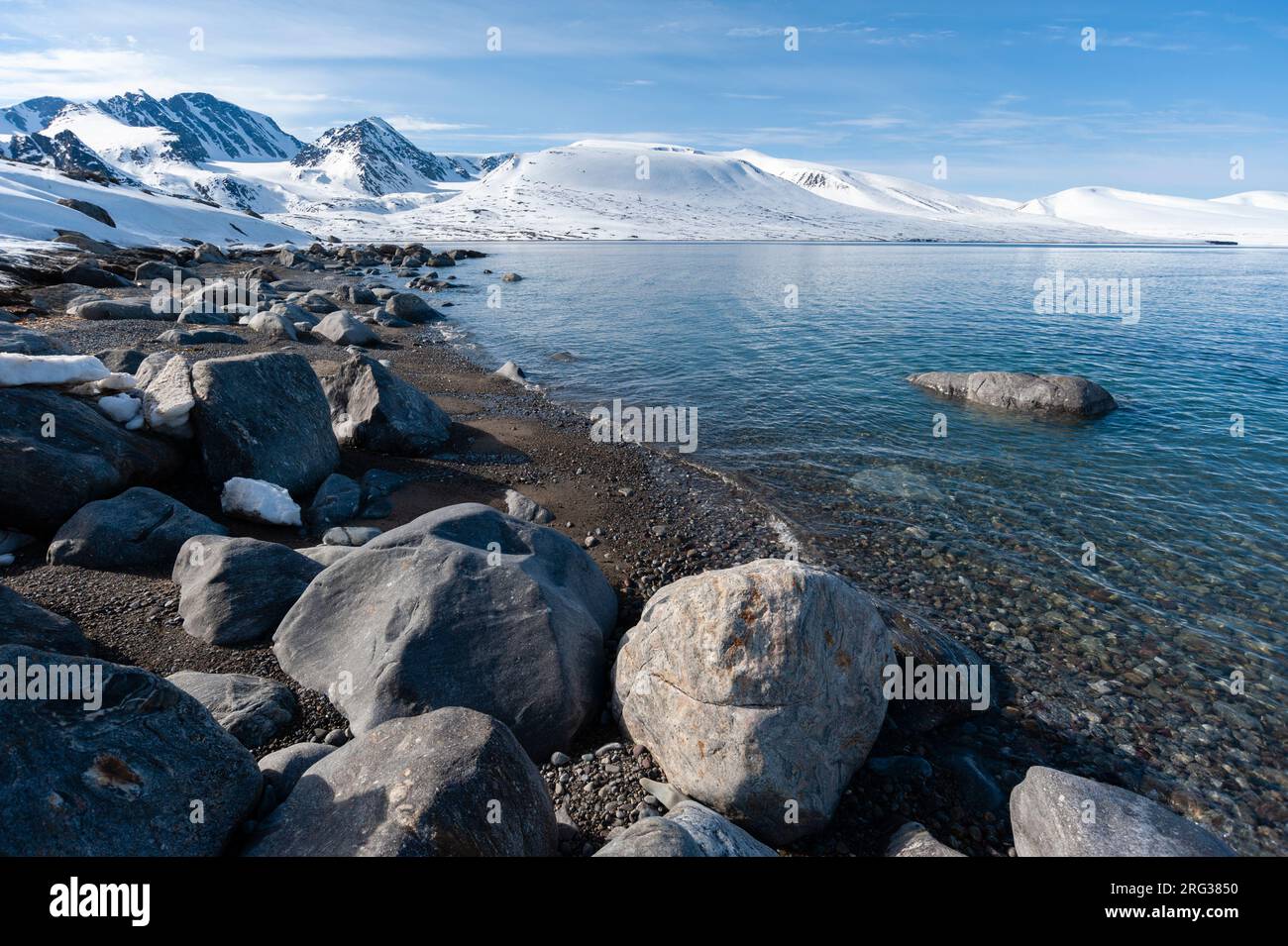A rocky beach and snow covered mountains border Bockfjorden ...