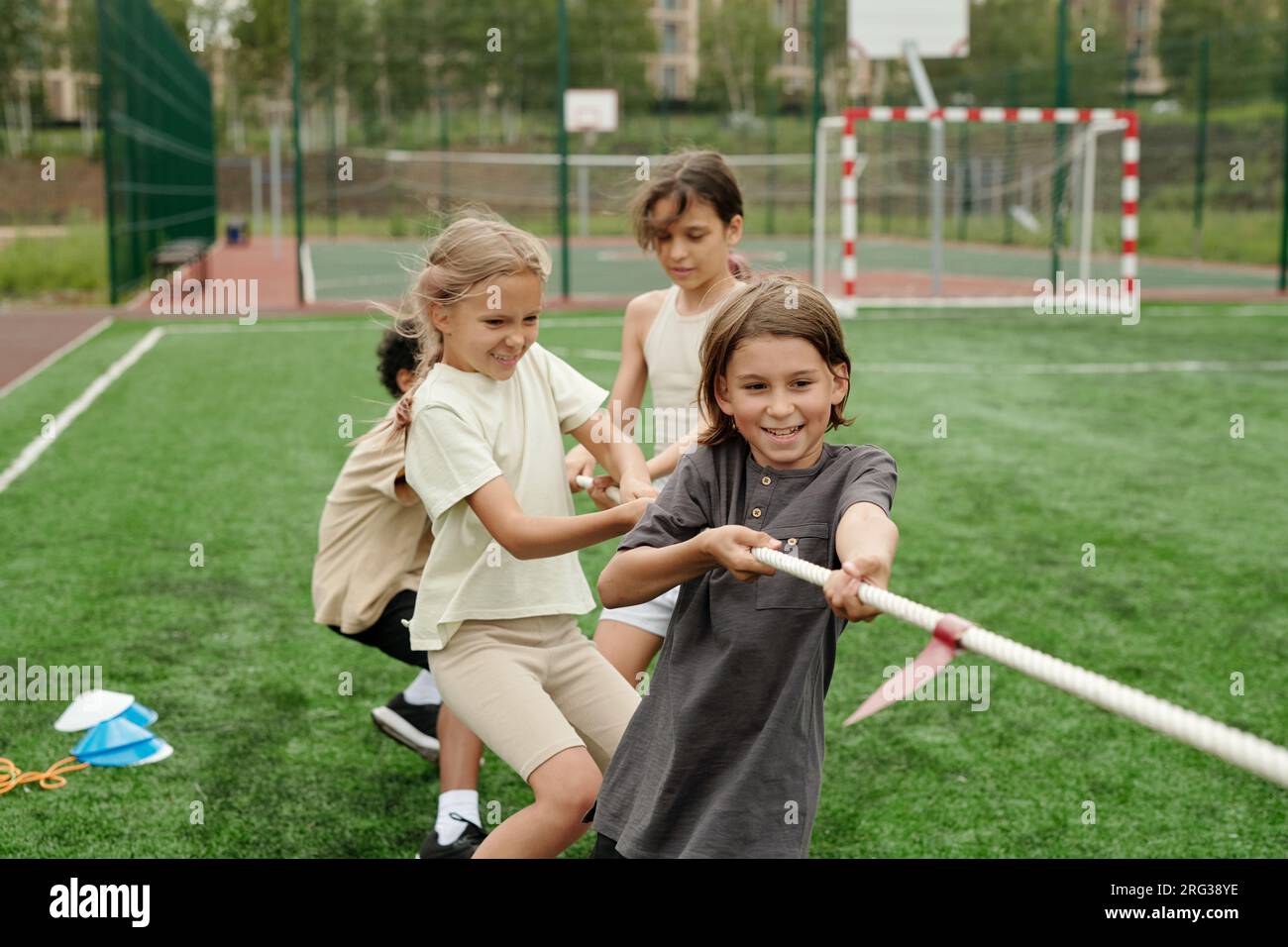 Happy cute intercultural classmates in activewear pulling rope during ...