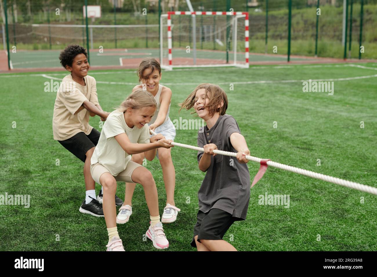 Cheerful schoolkids in activewear laughing while pulling rope during ...