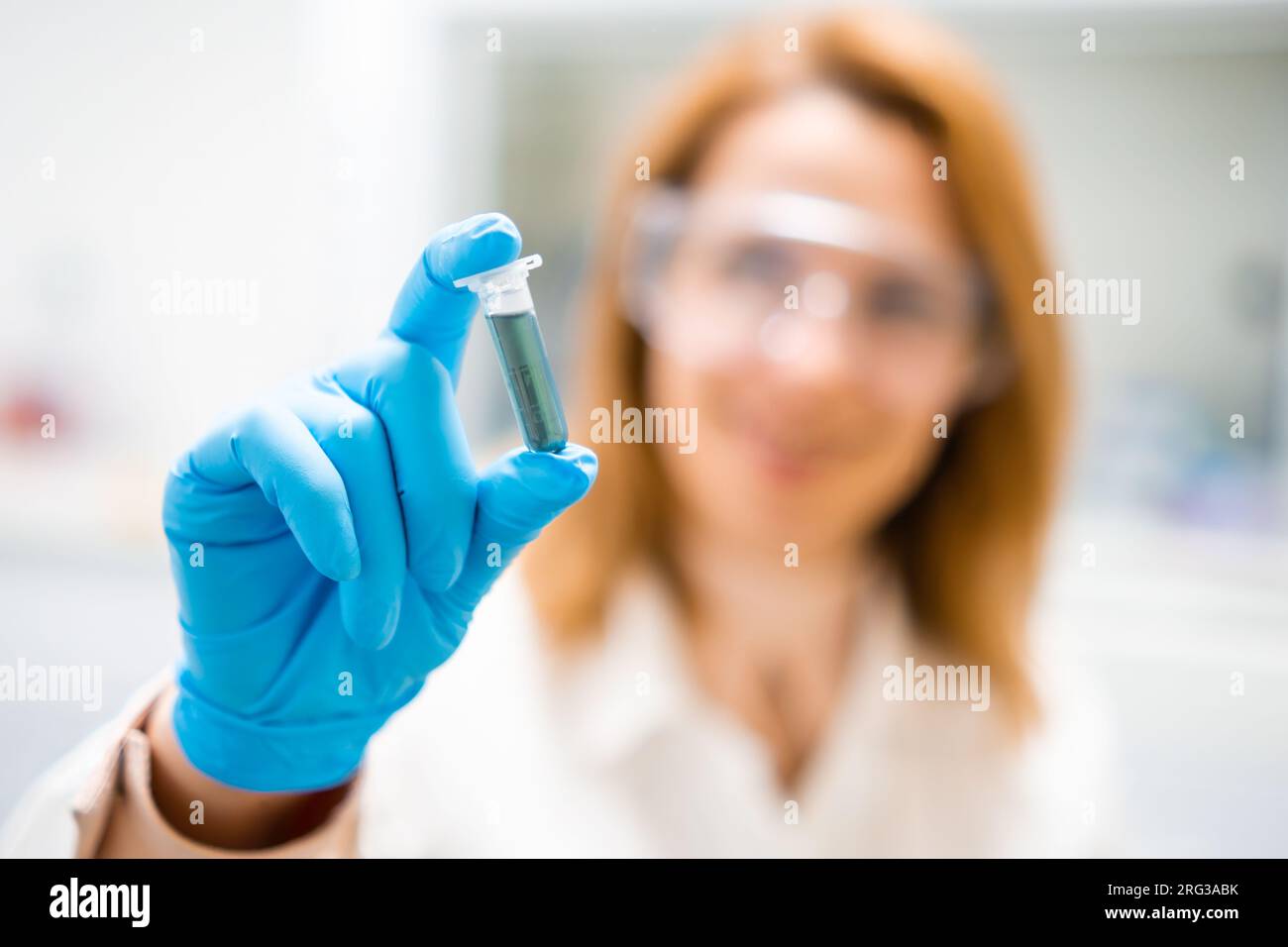 Hand of female scientist in rubber glove shaking test tube with blue ...
