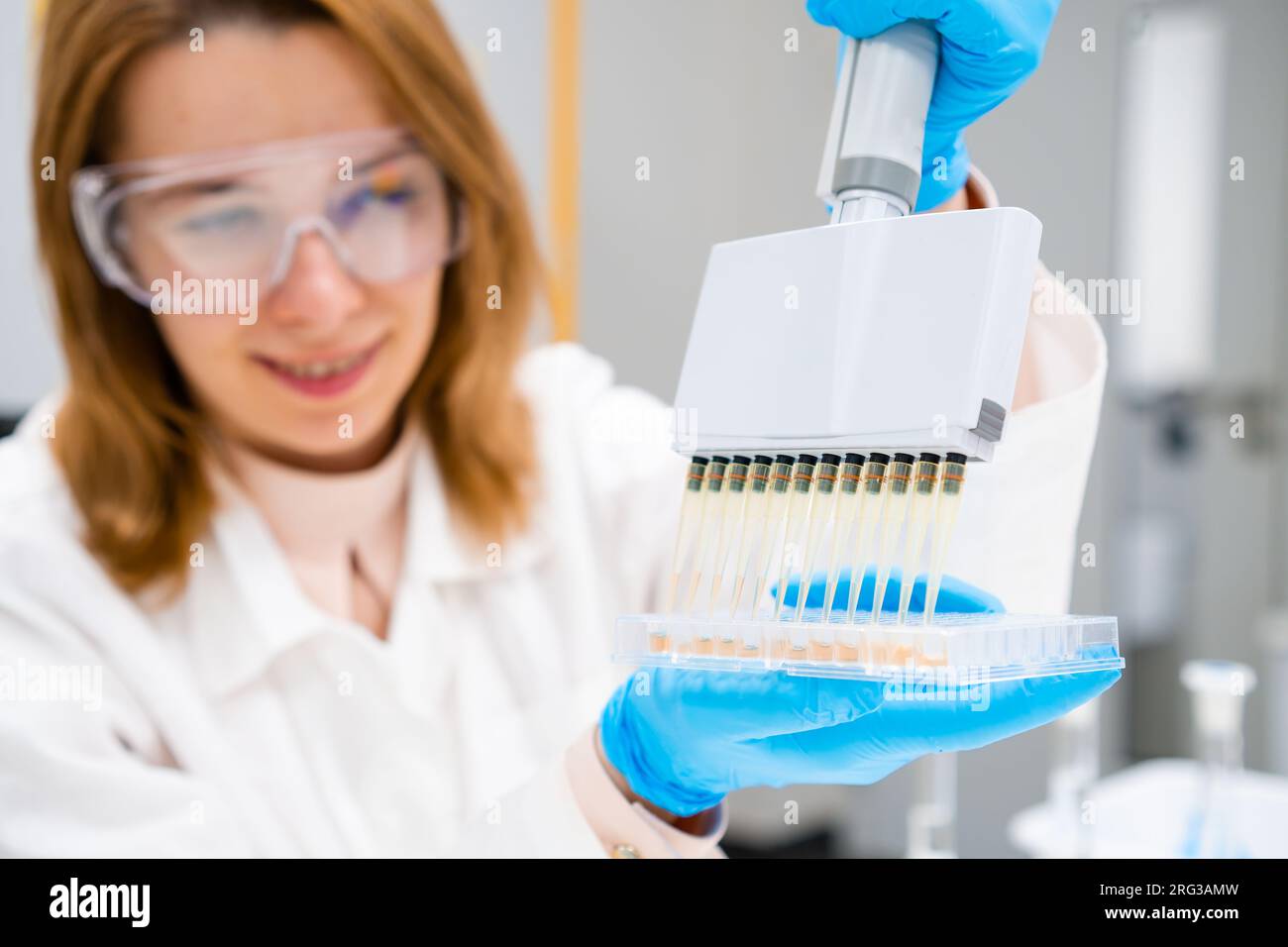 Scientist in goggles and rubber gloves uses pipette for filling 96 well plate for ...