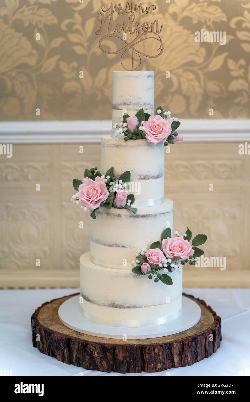 A delicious pink-frosted cake with fresh roses adorning the top sits ...