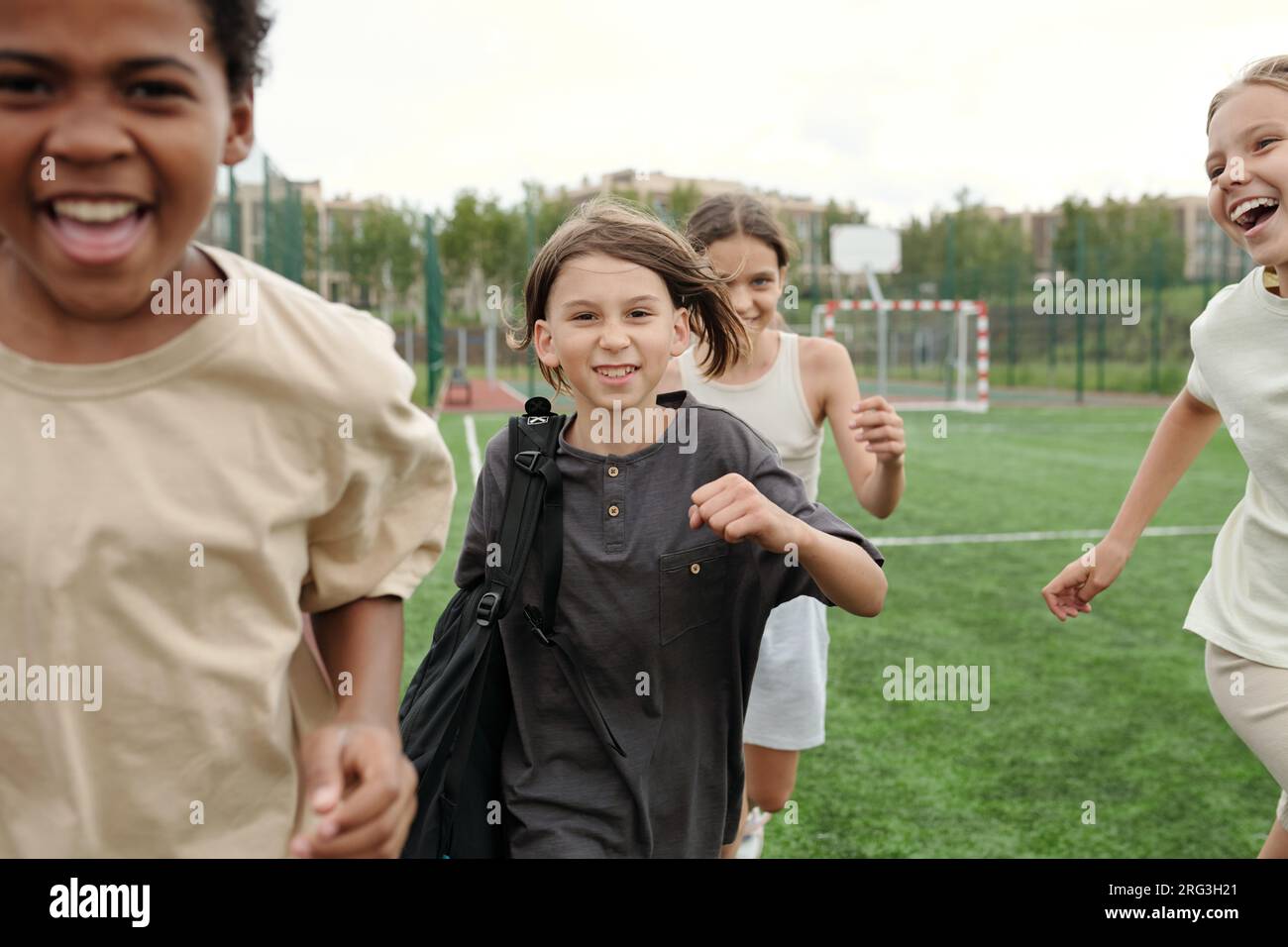 Happy blond schoolboy and two cheerful girls running after African ...