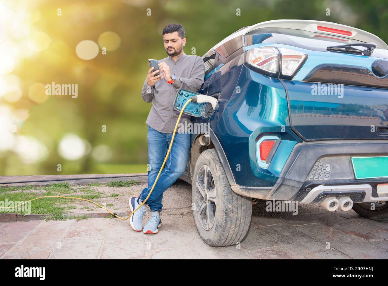 Happy Indian man using smartphone while his modern electric car getting ...