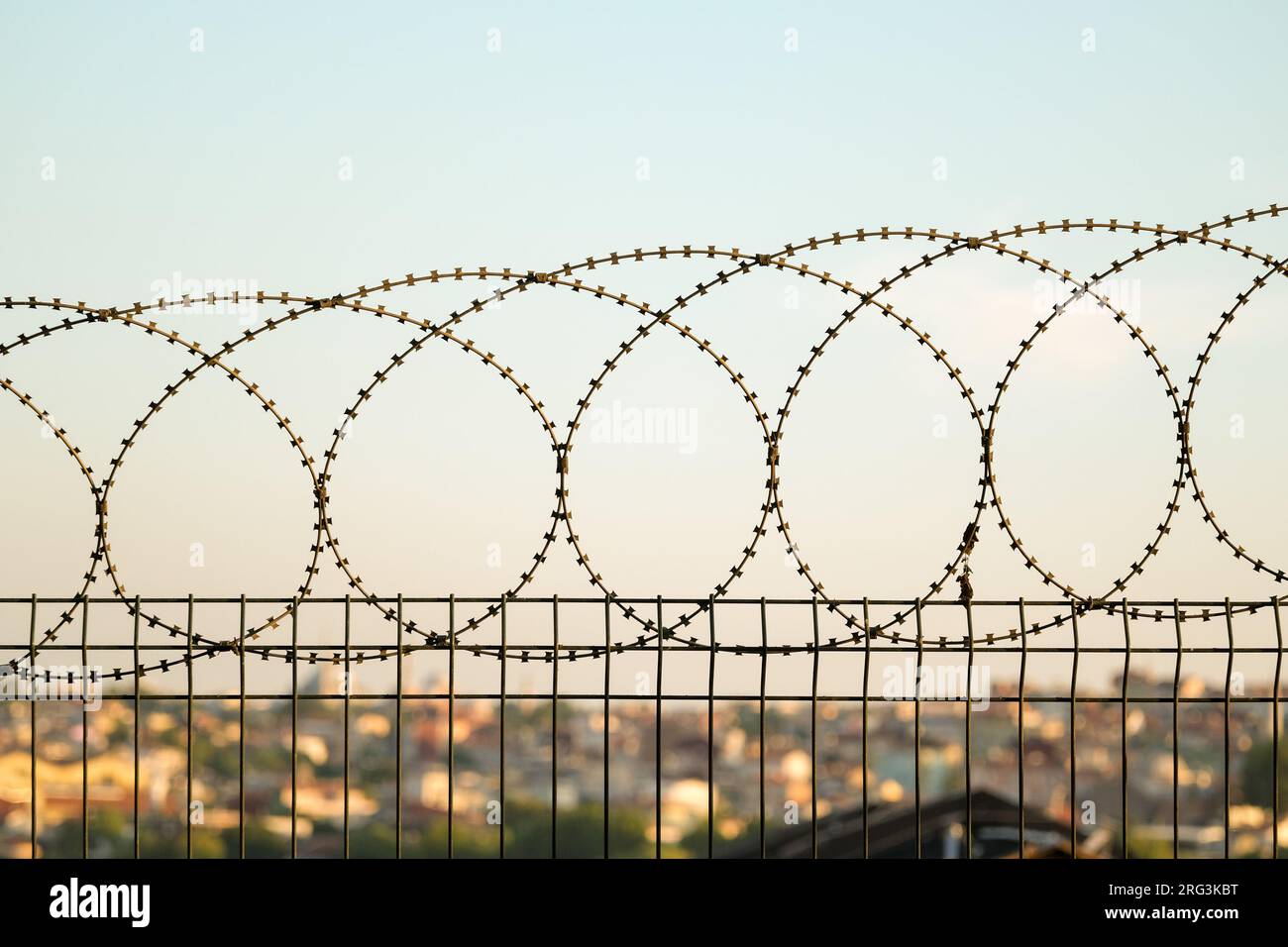 Close up barbed razor wire barrier against houses and blue sky ...