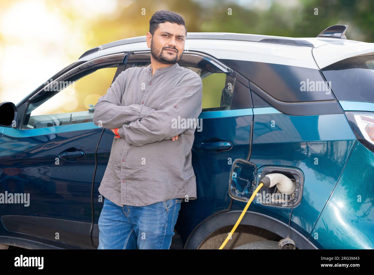 Indian man standing while his modern electric car getting charge at ...