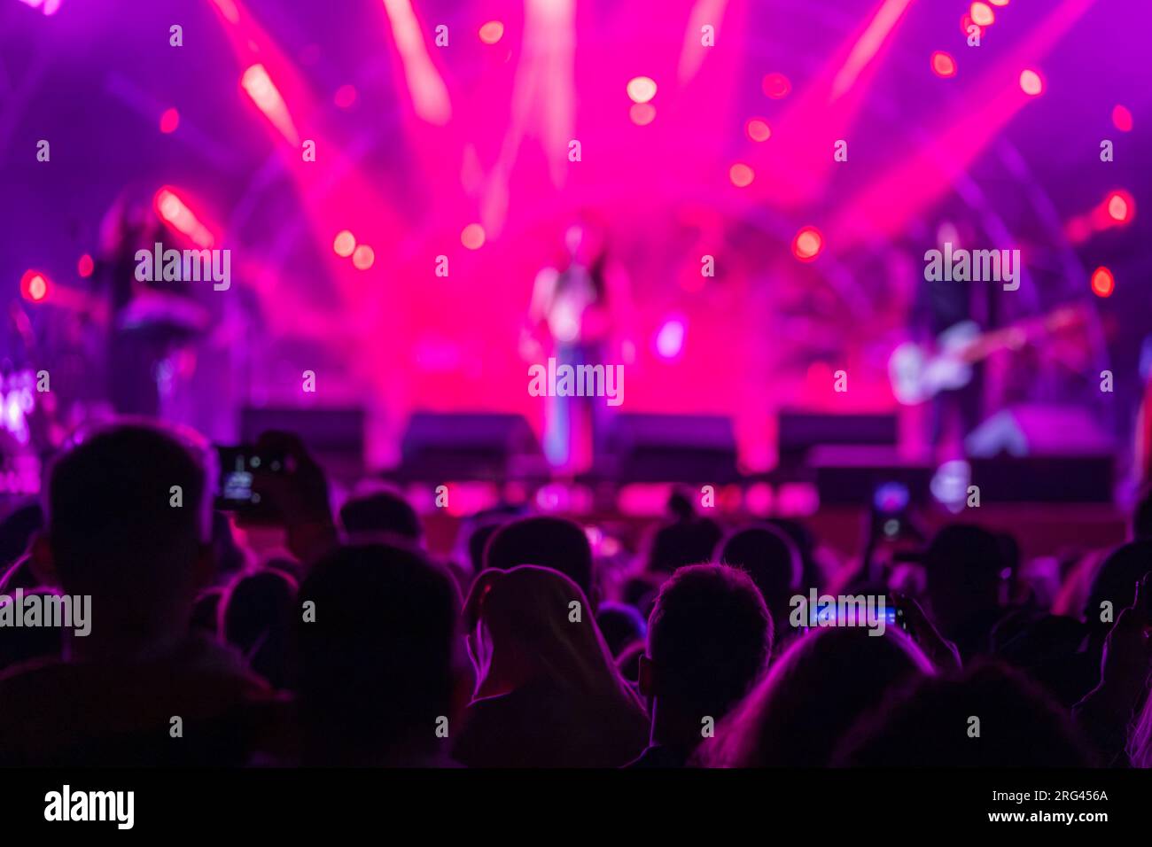 Crowd of fans near stage with performing music band in glowing red ...