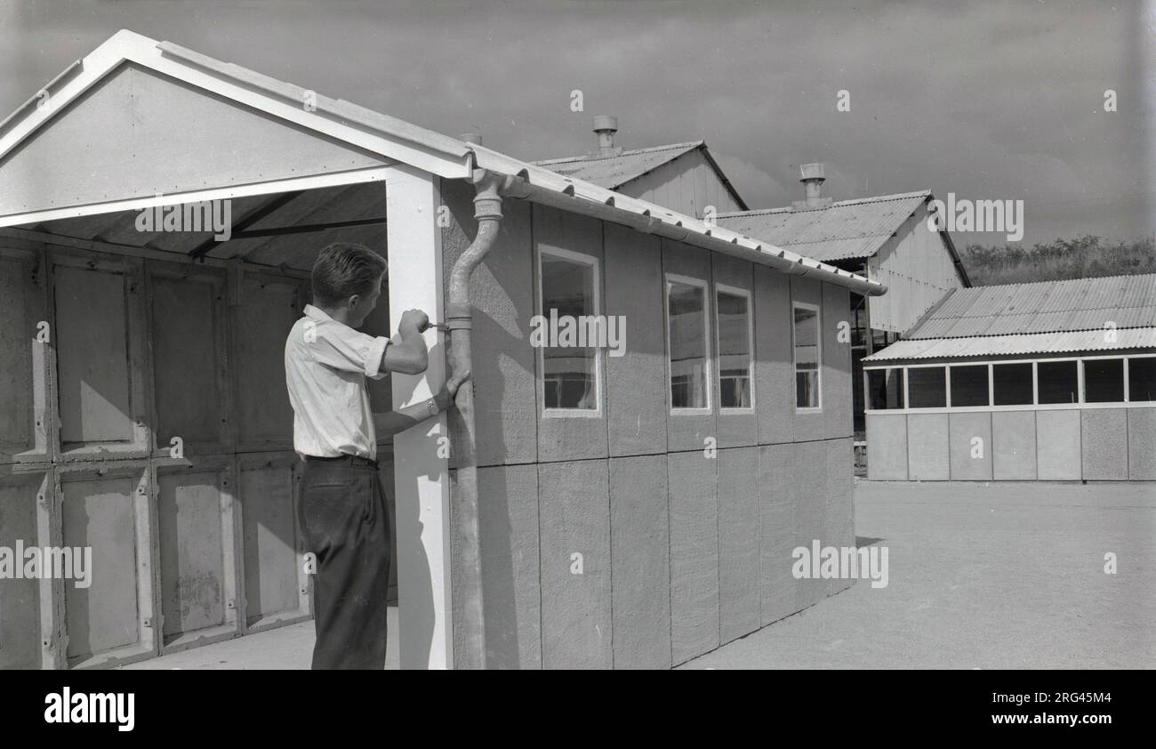 1950s, historical, a man fixing a bracket on the gutter on a prefab ...