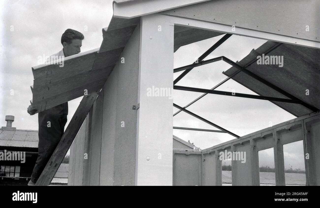 1950s, historical, a man standing on a ladder installing a roof panel ...
