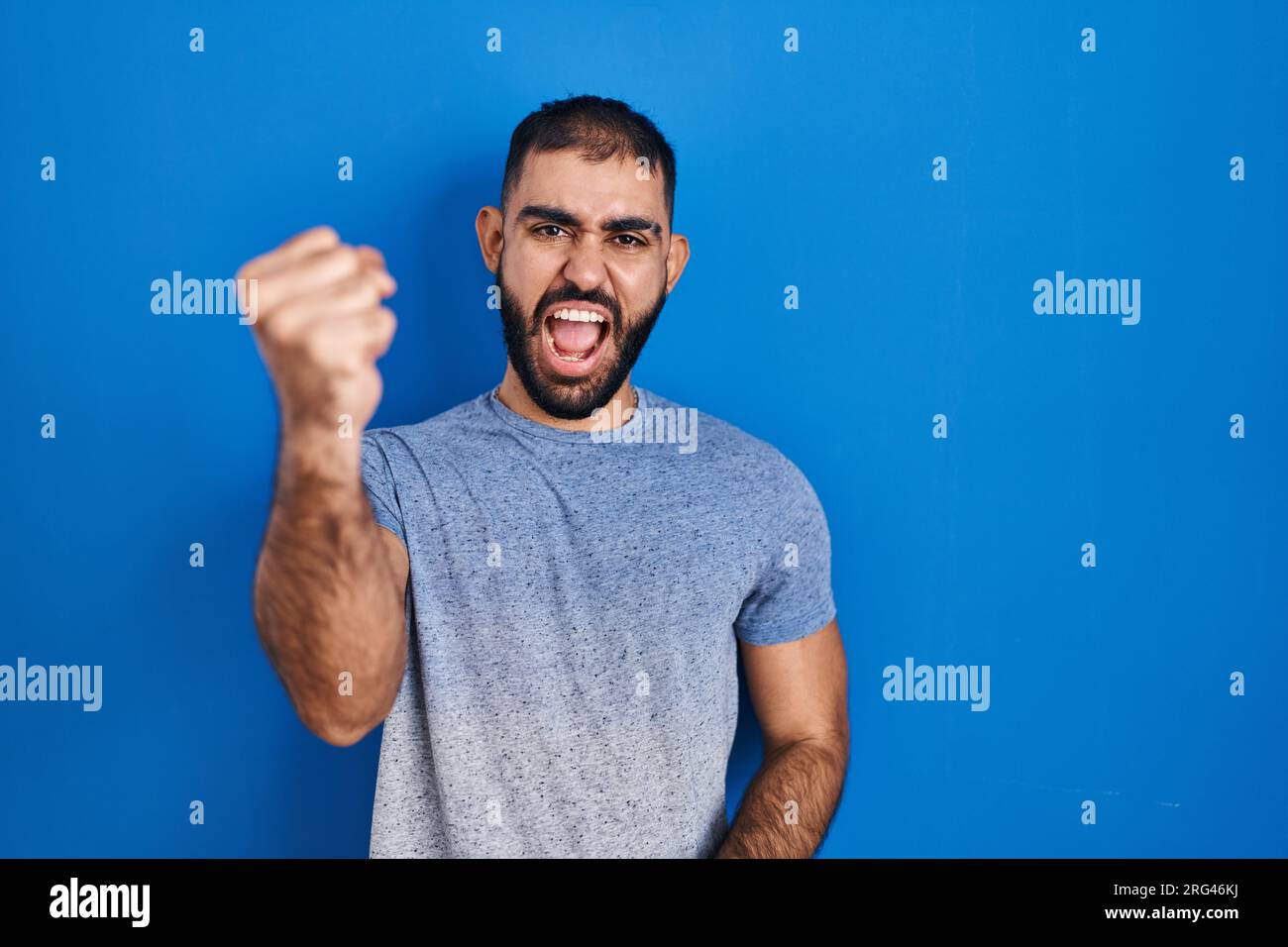 Middle east man with beard standing over blue background angry and mad ...