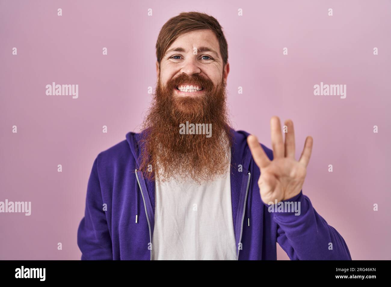 Caucasian man with long beard standing over pink background showing and ...