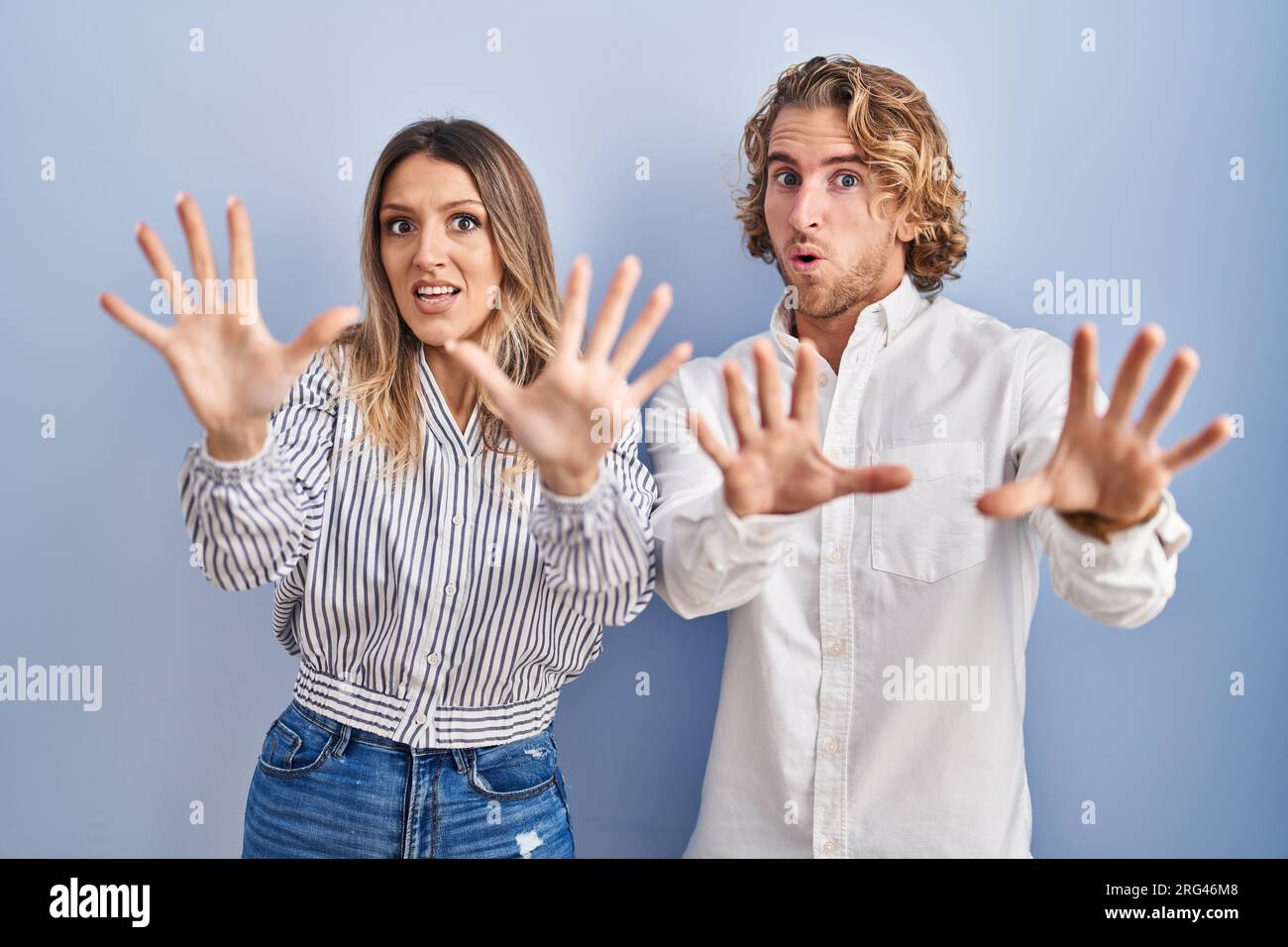 Young couple standing over blue background afraid and terrified with ...