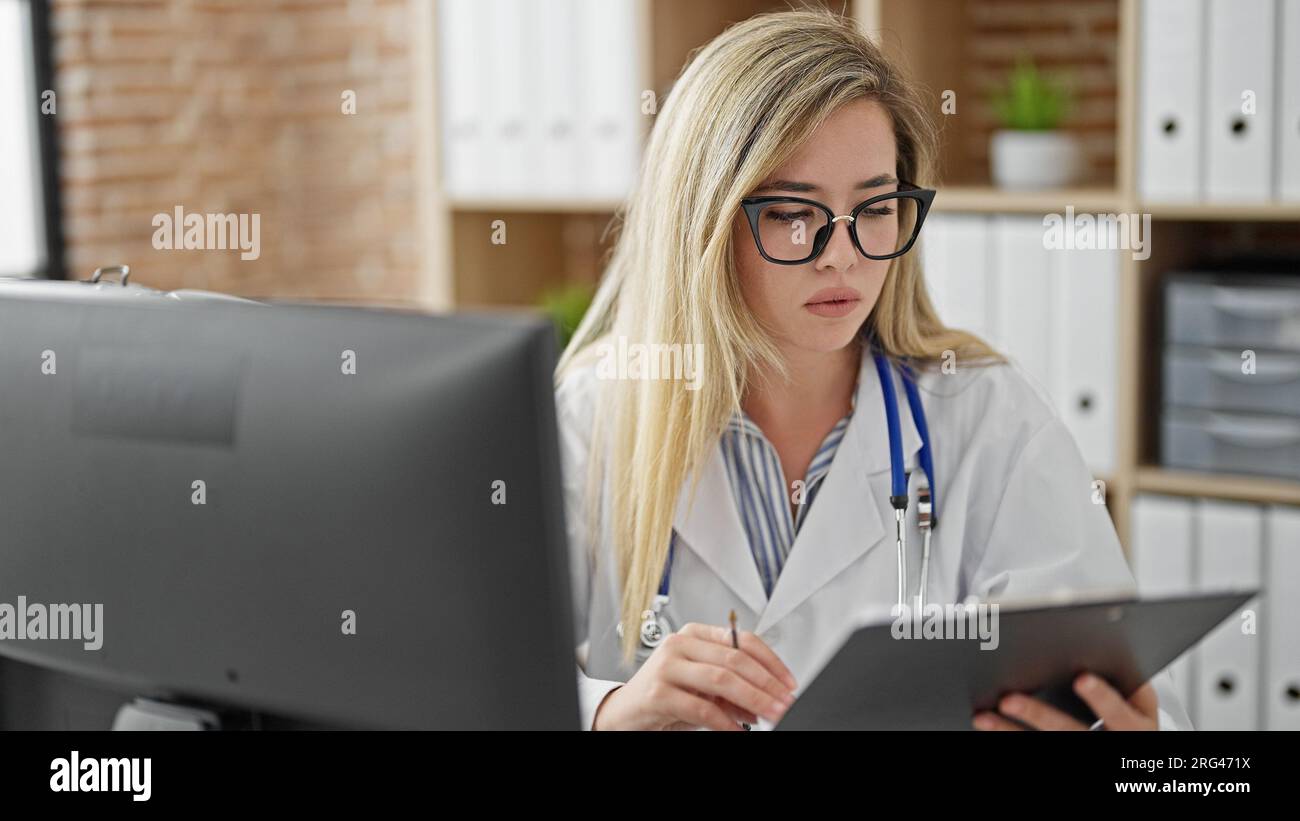 Young blonde woman doctor using computer reading medical report at ...