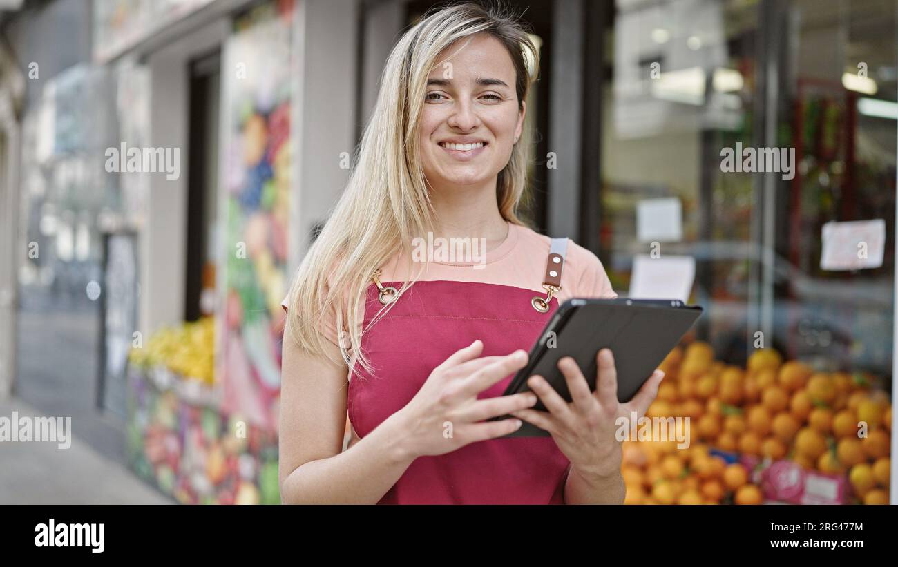 Young blonde woman shop assistant smiling confident using touchpad at ...