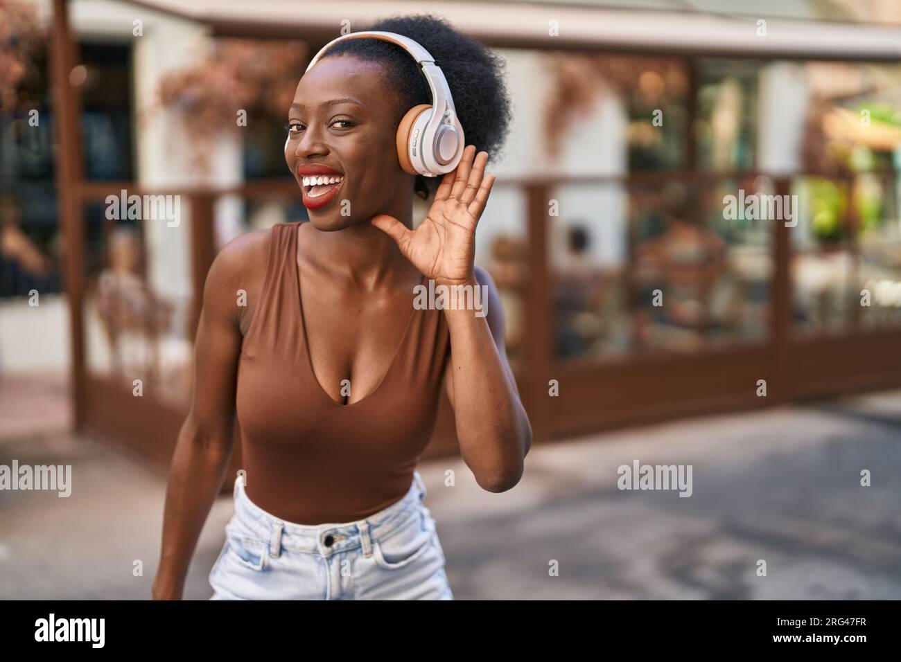 African woman with curly hair outdoors at the city wearing headphones ...