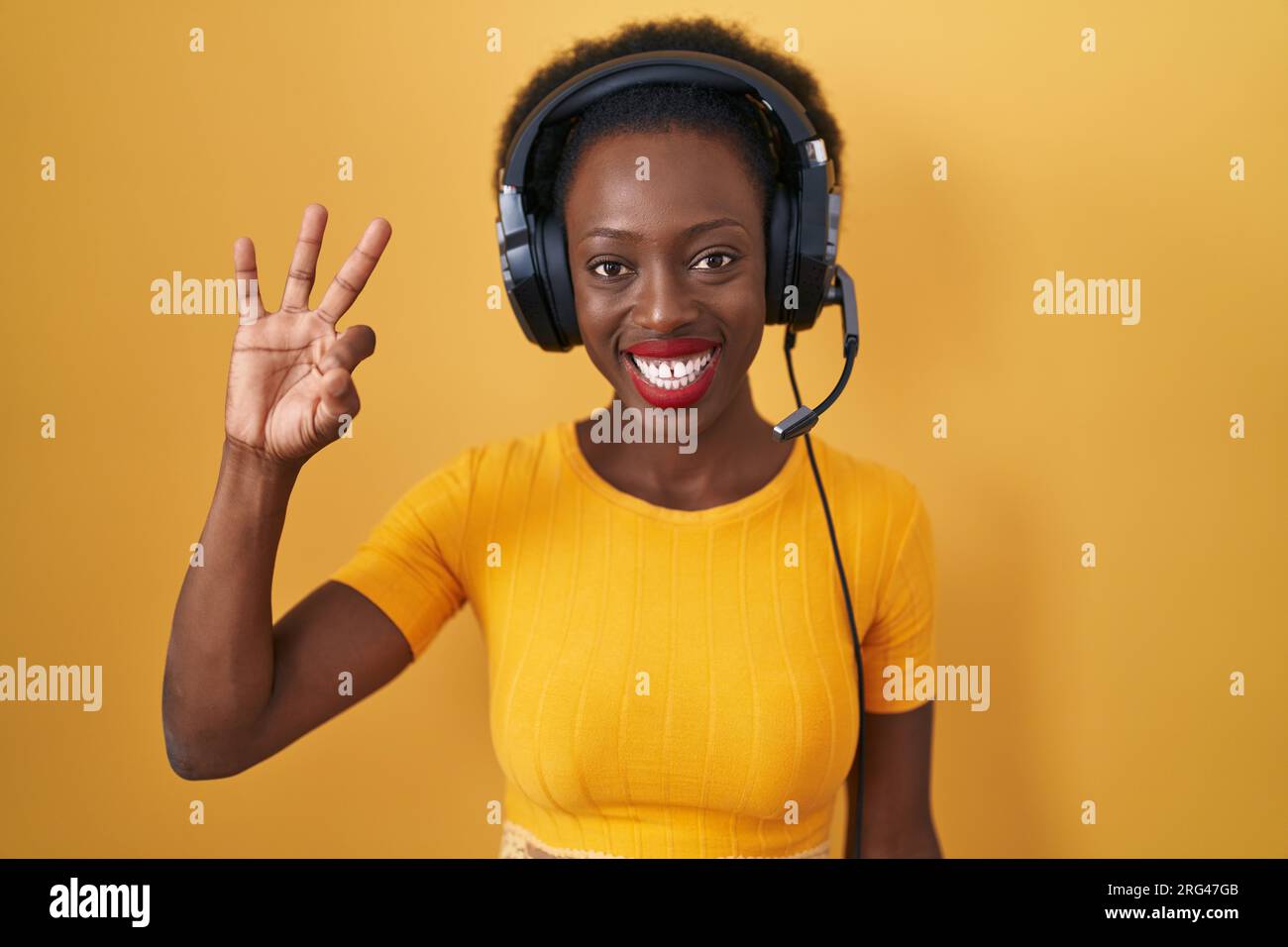 African woman with curly hair standing over yellow background wearing ...