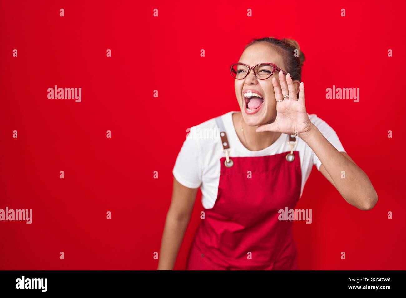 Young hispanic woman wearing waitress apron over red background ...