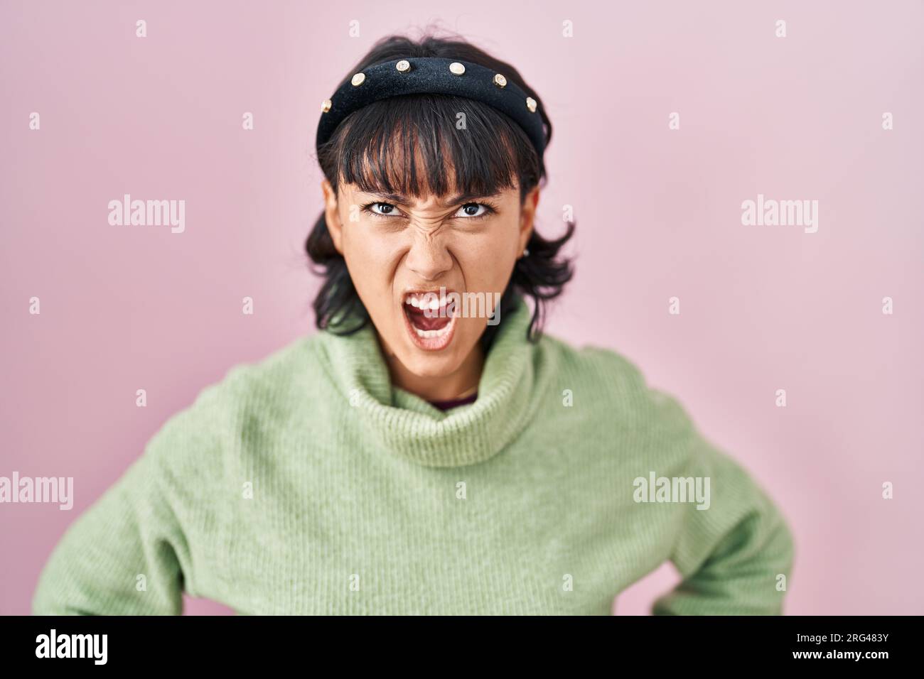 Young beautiful woman standing over pink background angry and mad ...