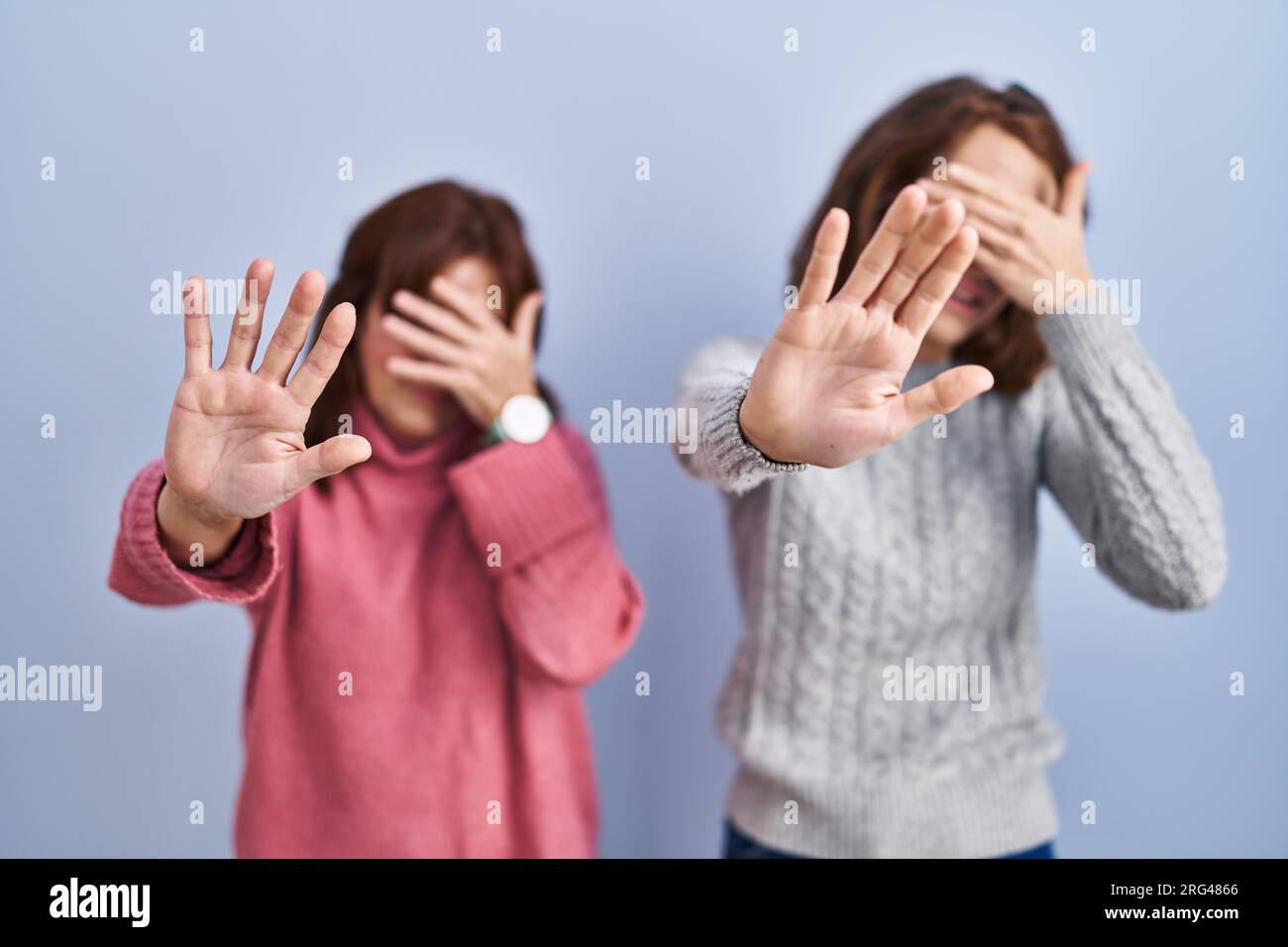 Mother and daughter standing over blue background covering eyes with ...