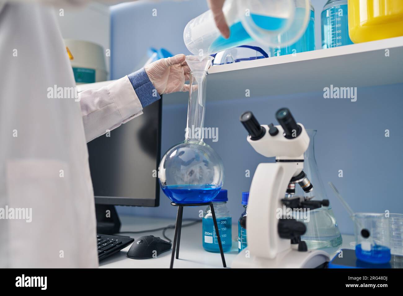 Young blonde woman scientist pouring liquid on test tube at laboratory ...