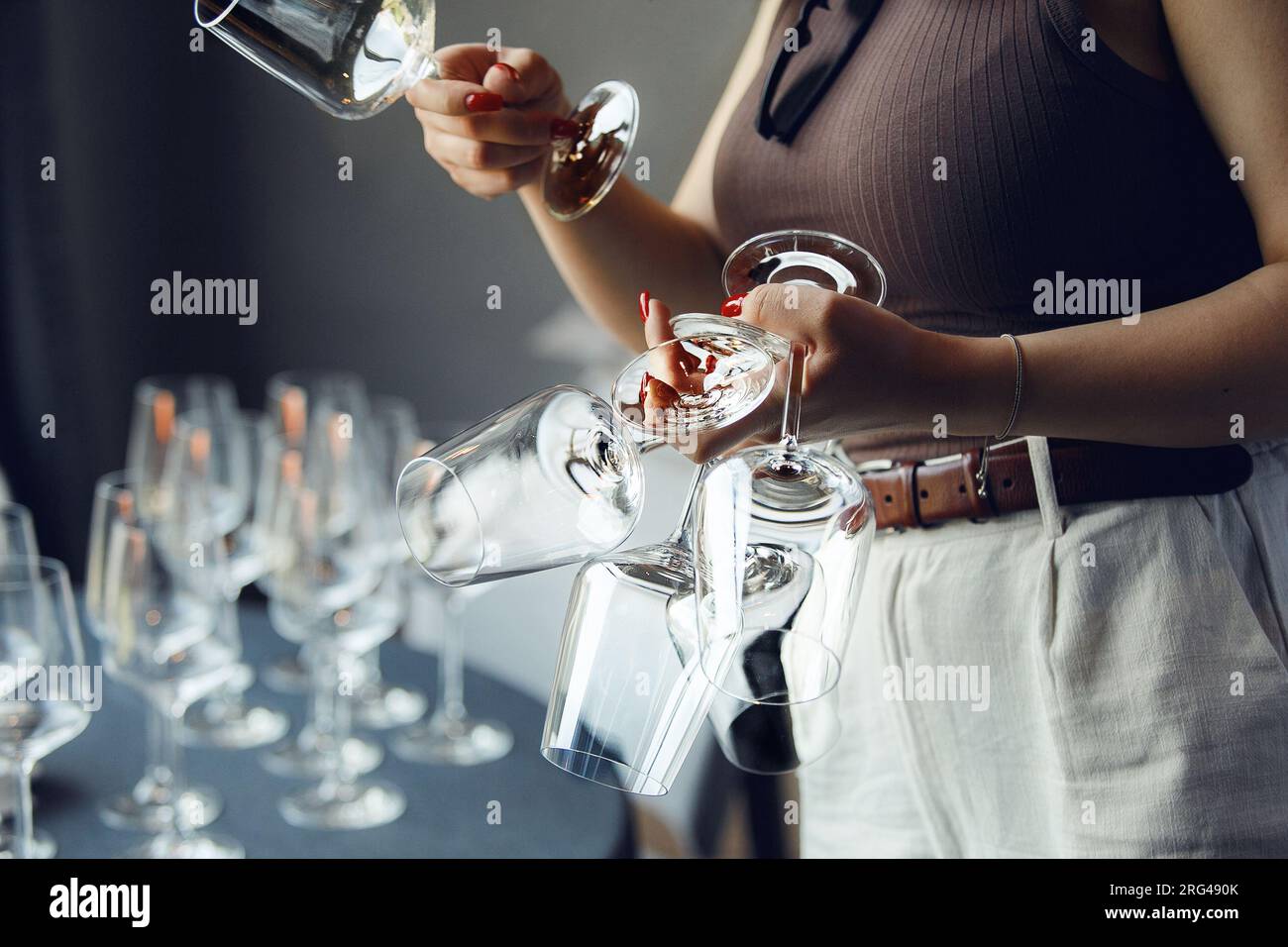 Female waiter takes several empty wine glasses from the bar table and ...