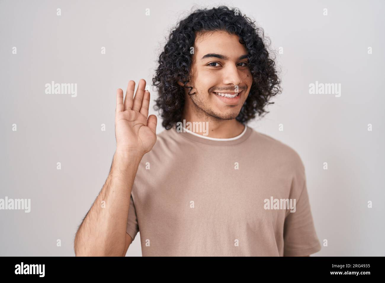 Hispanic man with curly hair standing over white background waiving ...
