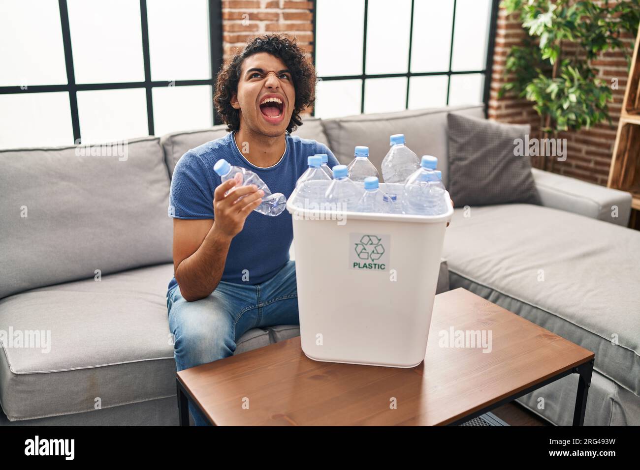 Hispanic man with curly hair holding recycling bin with plastic bottles ...