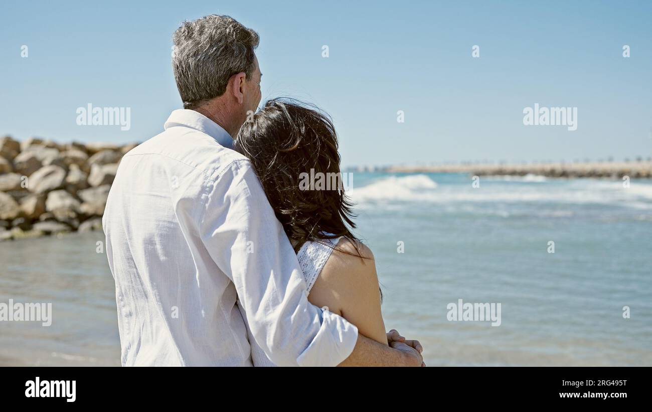 Senior man and woman couple hugging each other backwards at seaside ...