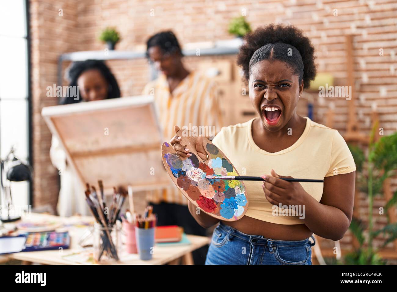 Young black painter woman at art studio holding palette angry and mad ...