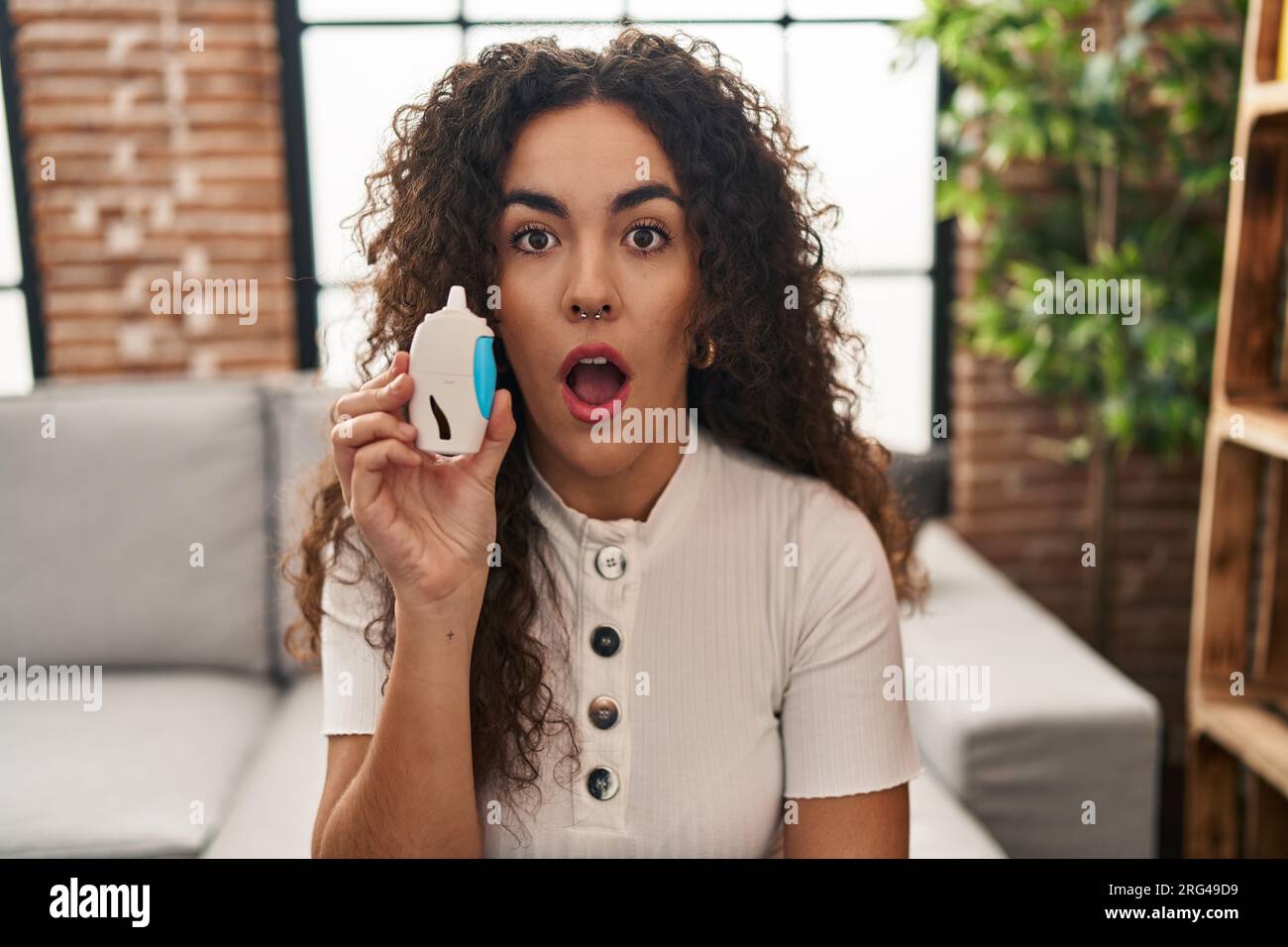 Young hispanic woman using glucose meter scared and amazed with open ...