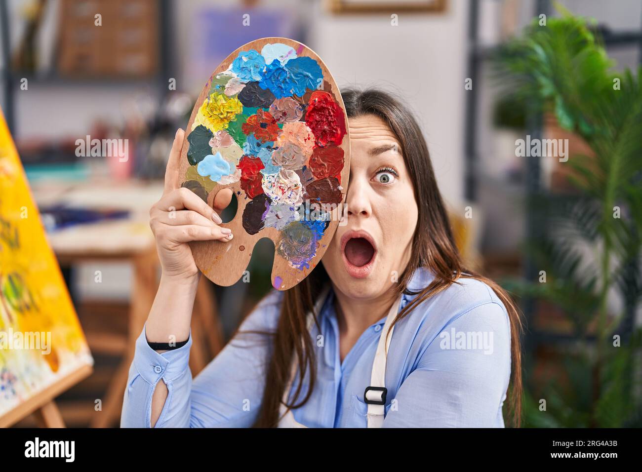 Young brunette woman covering face with painter palette afraid and ...