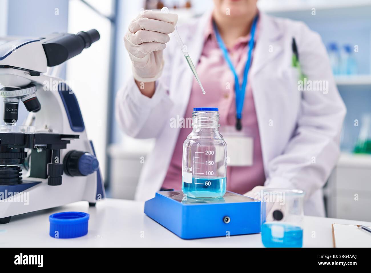 Young beautiful plus size woman scientist pouring liquid on test tube ...
