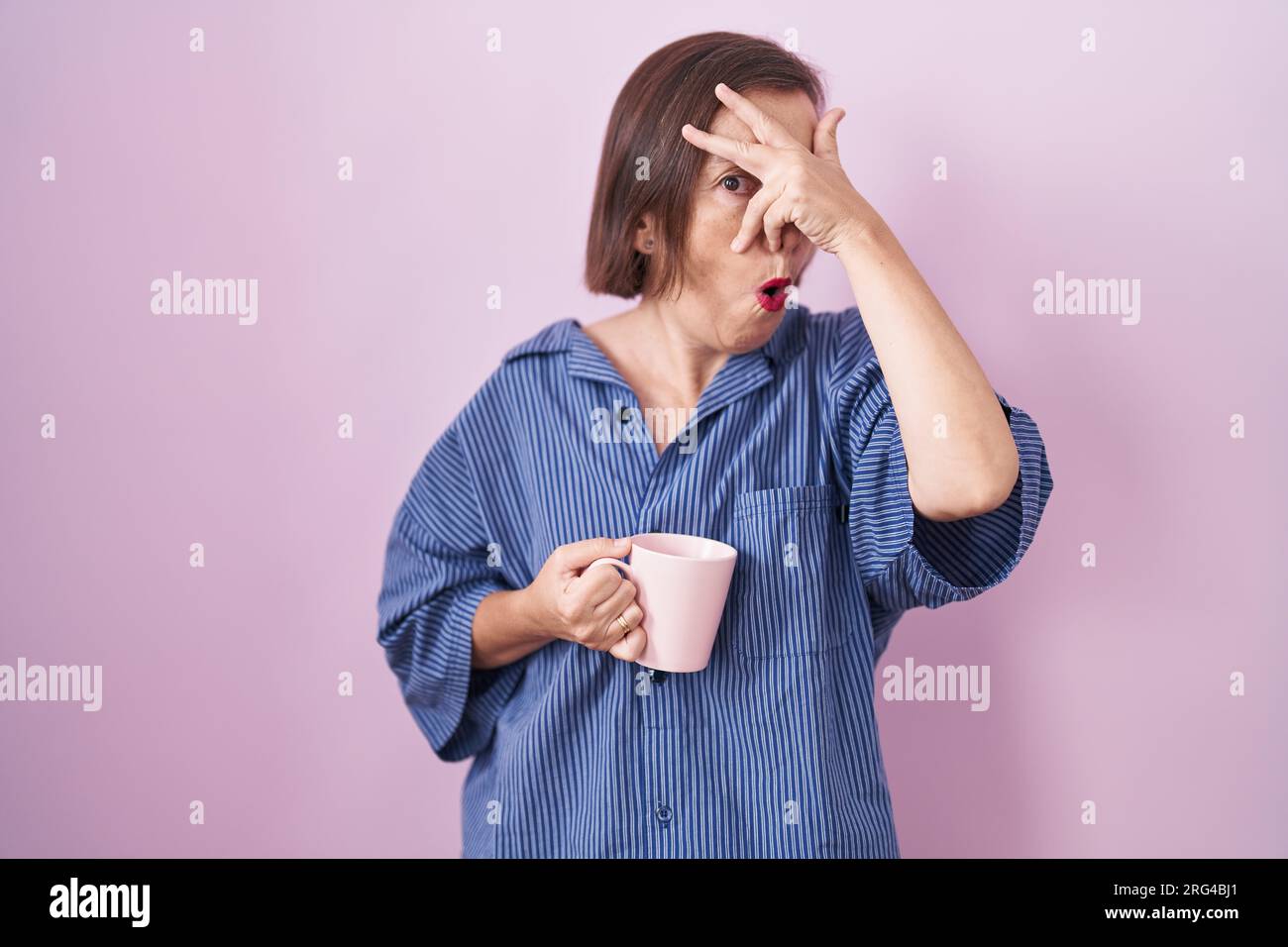 Middle age hispanic woman drinking a cup coffee peeking in shock ...