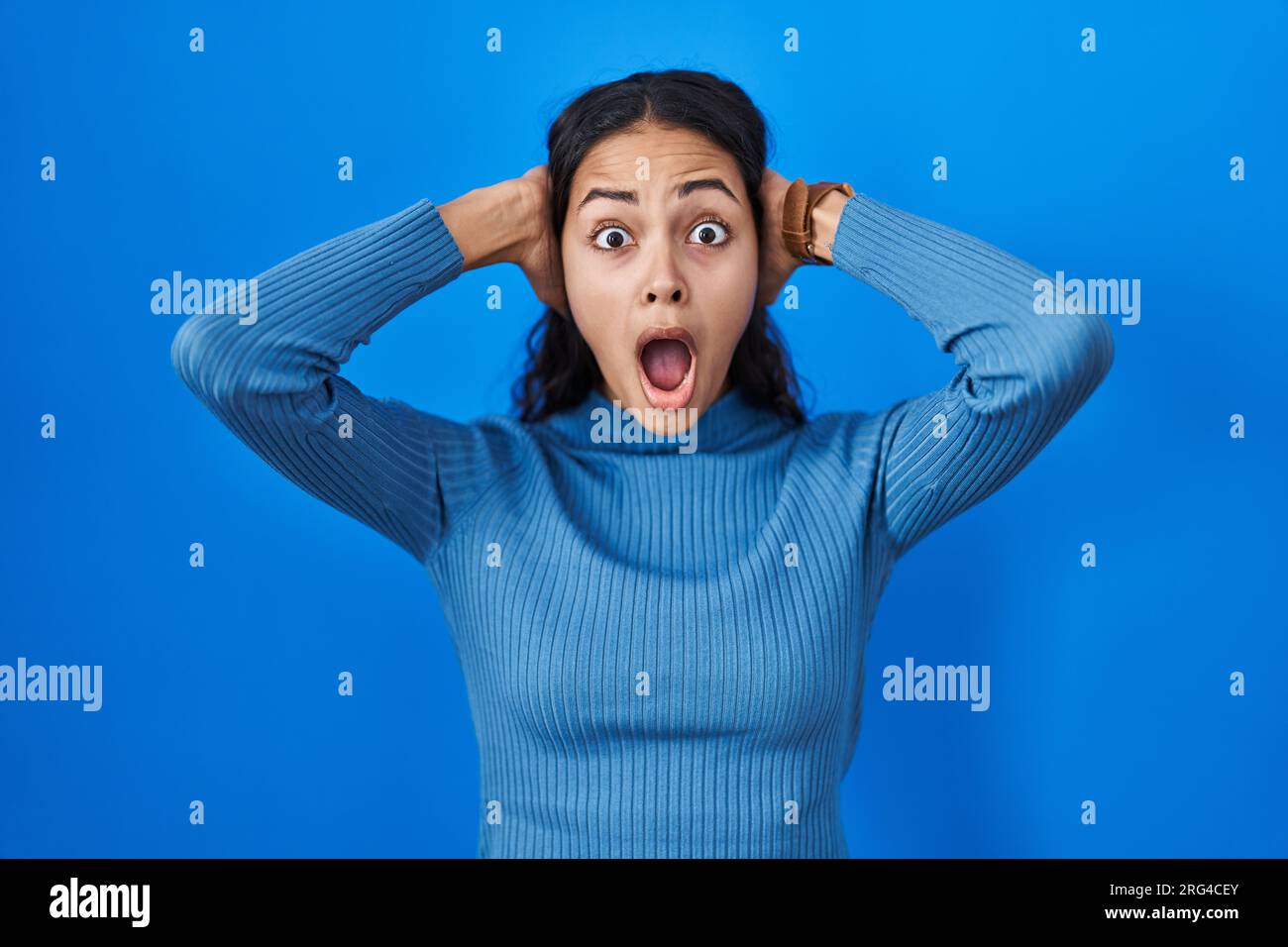 Young brazilian woman standing over blue isolated background crazy and ...