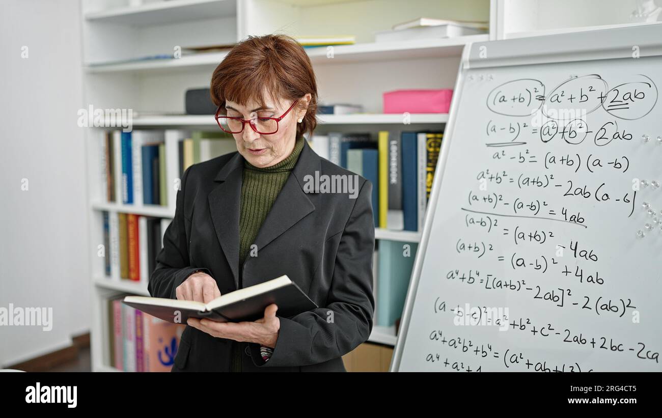 Mature hispanic woman teacher standing reading book at library university Stock Photo - Alamy