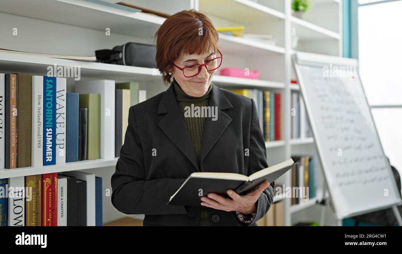 Mature hispanic woman teacher standing reading book at library university Stock Photo - Alamy