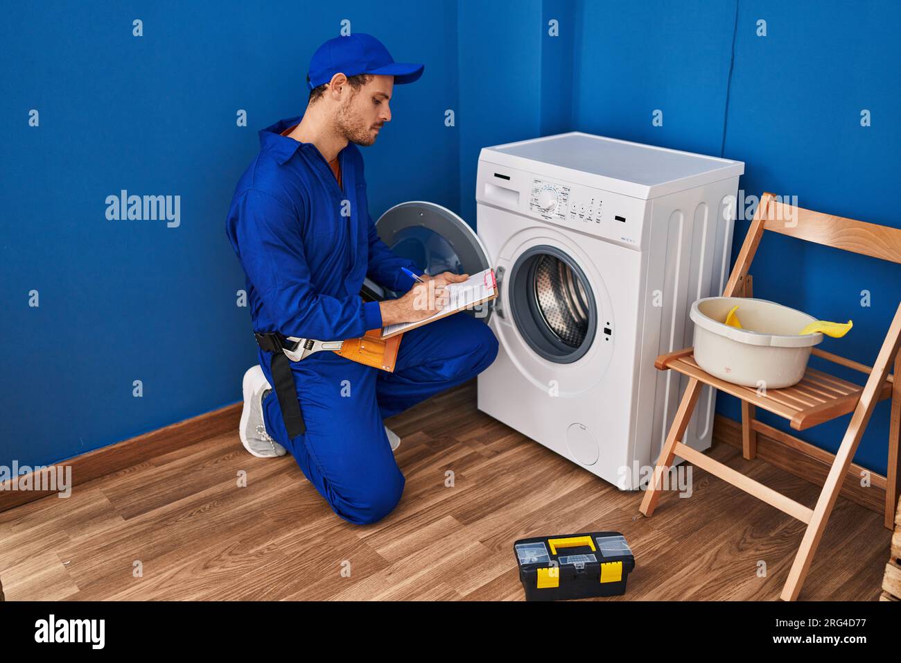 Young hispanic man technician repairing washing machine writing on ...