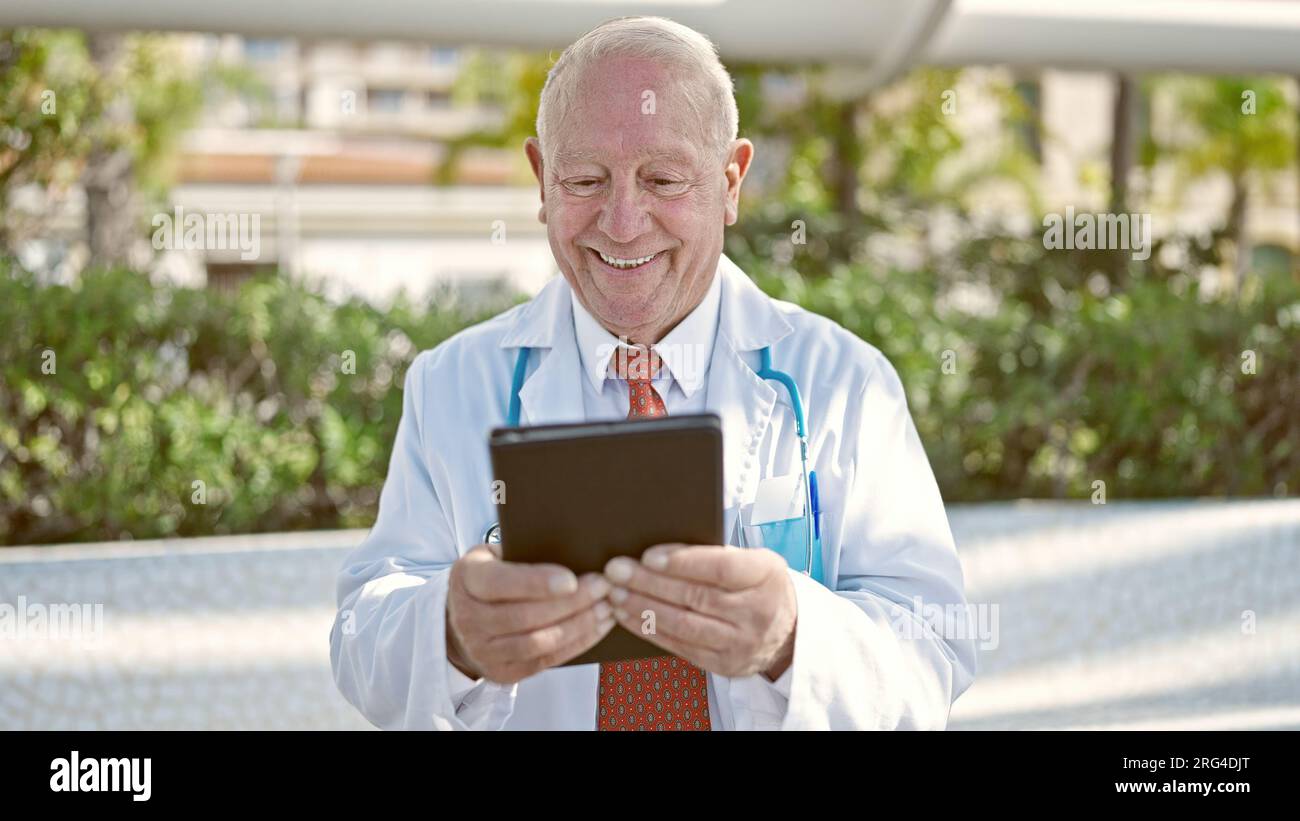 Senior grey-haired man doctor smiling confident using touchpad at park Stock Photo - Alamy