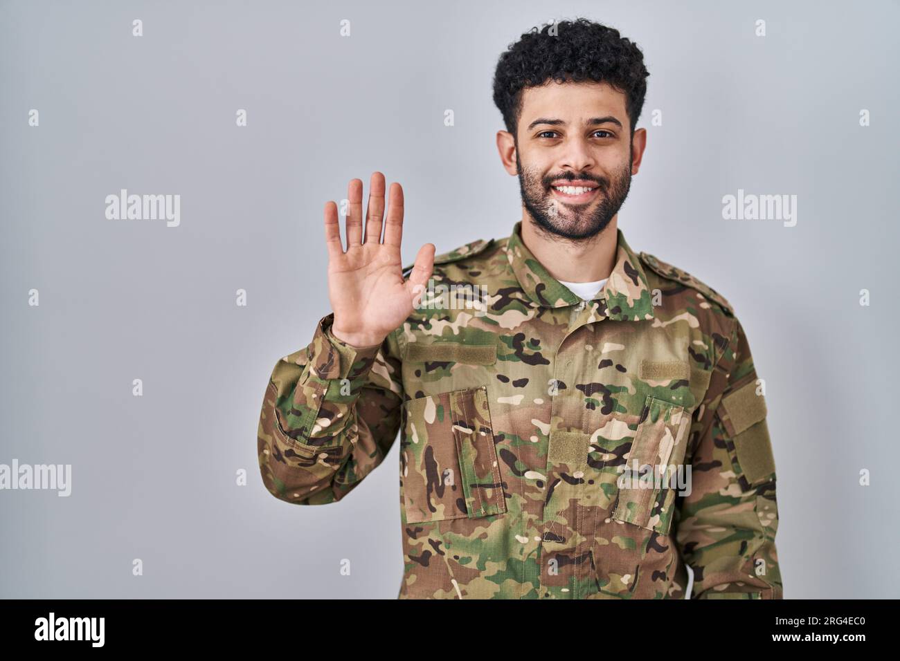 Arab man wearing camouflage army uniform waiving saying hello happy and ...