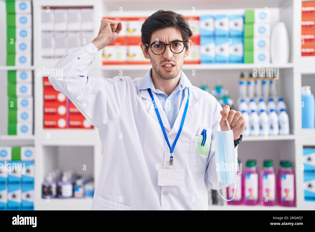Young hispanic man working at pharmacy drugstore holding safety mask ...