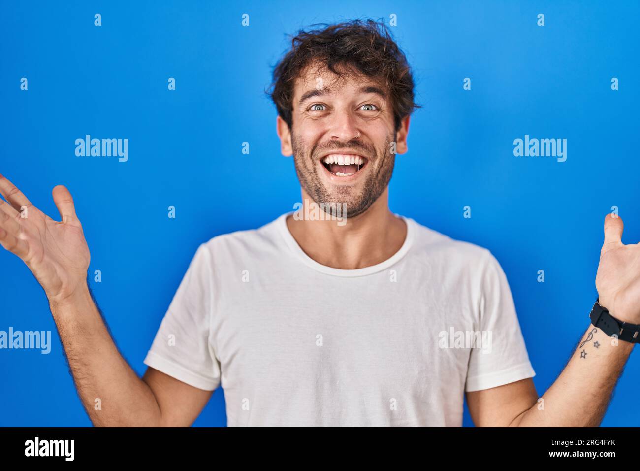 Hispanic young man standing over blue background celebrating crazy and ...