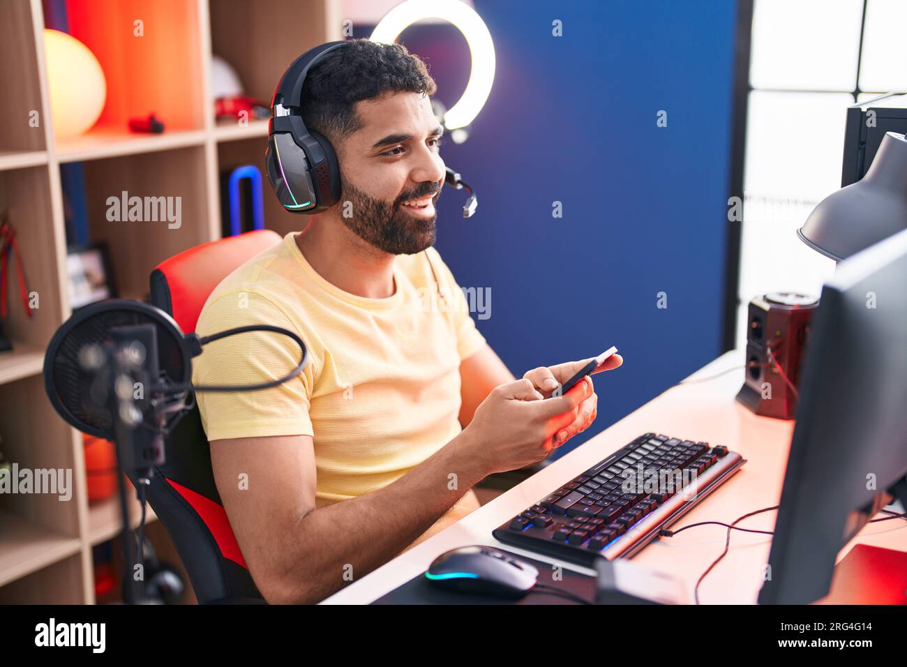 Young arab man streamer using computer and smartphone at gaming room ...