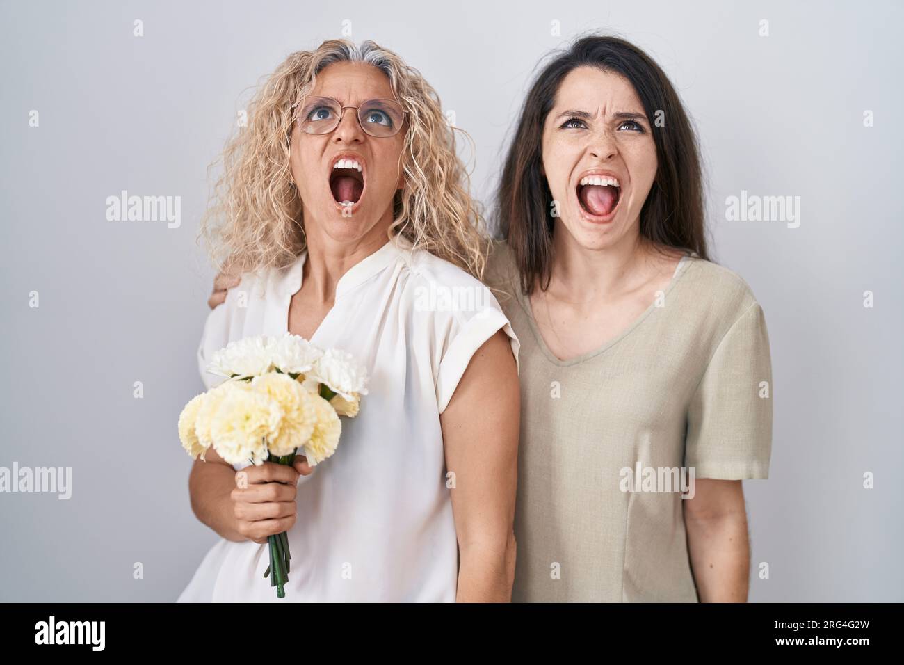 Mother and daughter holding bouquet of white flowers angry and mad ...