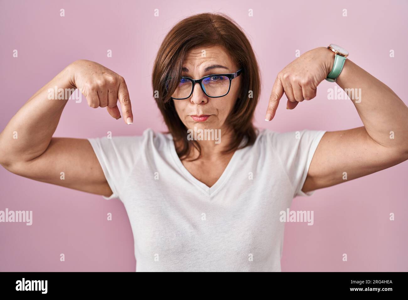 Middle age hispanic woman standing over pink background pointing down ...
