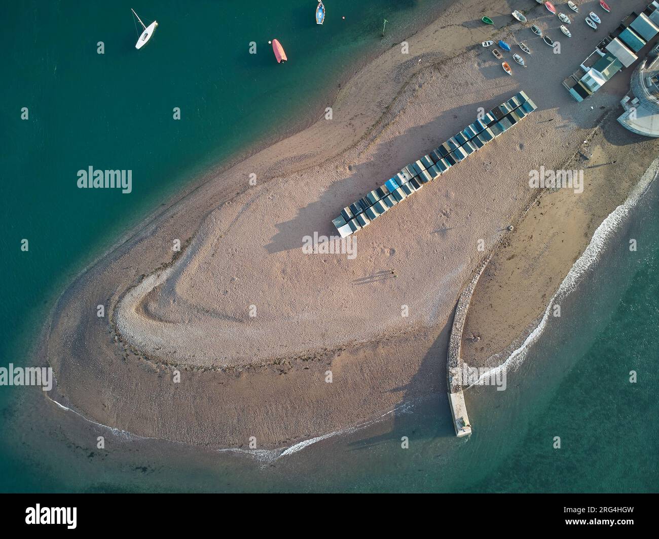A river mouth sandbar, with beach huts on the sand, boats moored in the ...